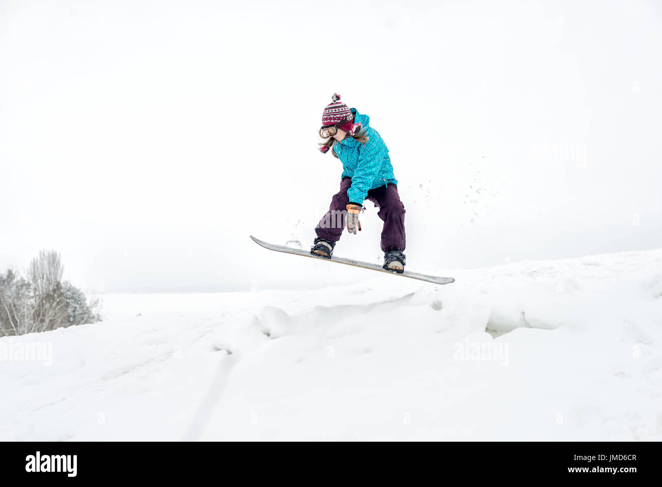 pretty young woman on the snowboard jumping over the slope in winter ...