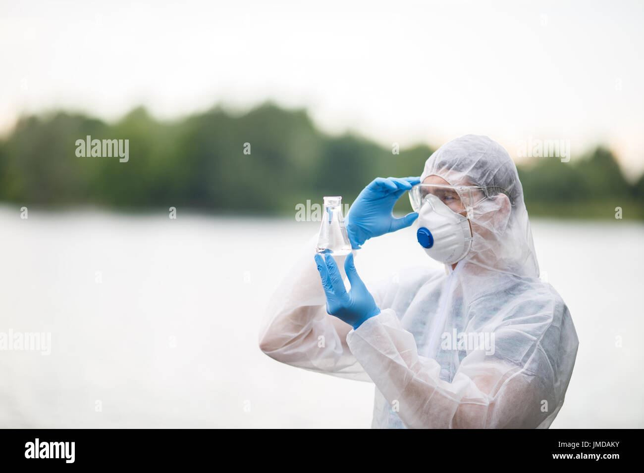 Chemist in safety glasses and respirator holds flask with water in ...