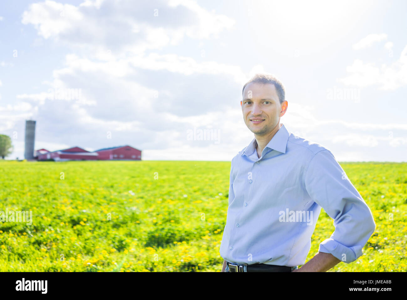 Young man standing in vast, open summer countryside field by red ...