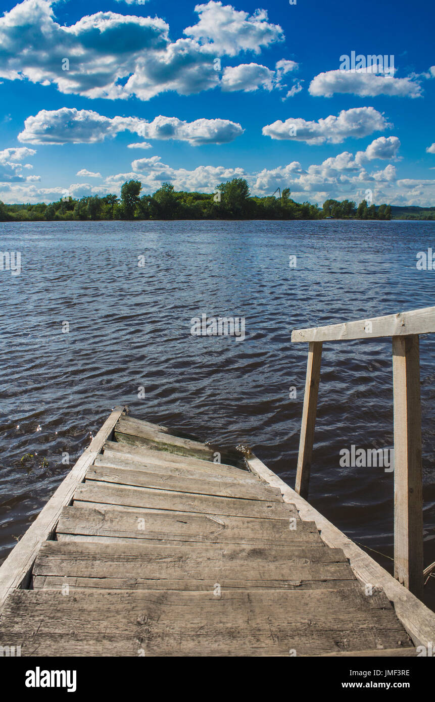 Wooden steps for boarding a boat go into the water under a blue sky ...