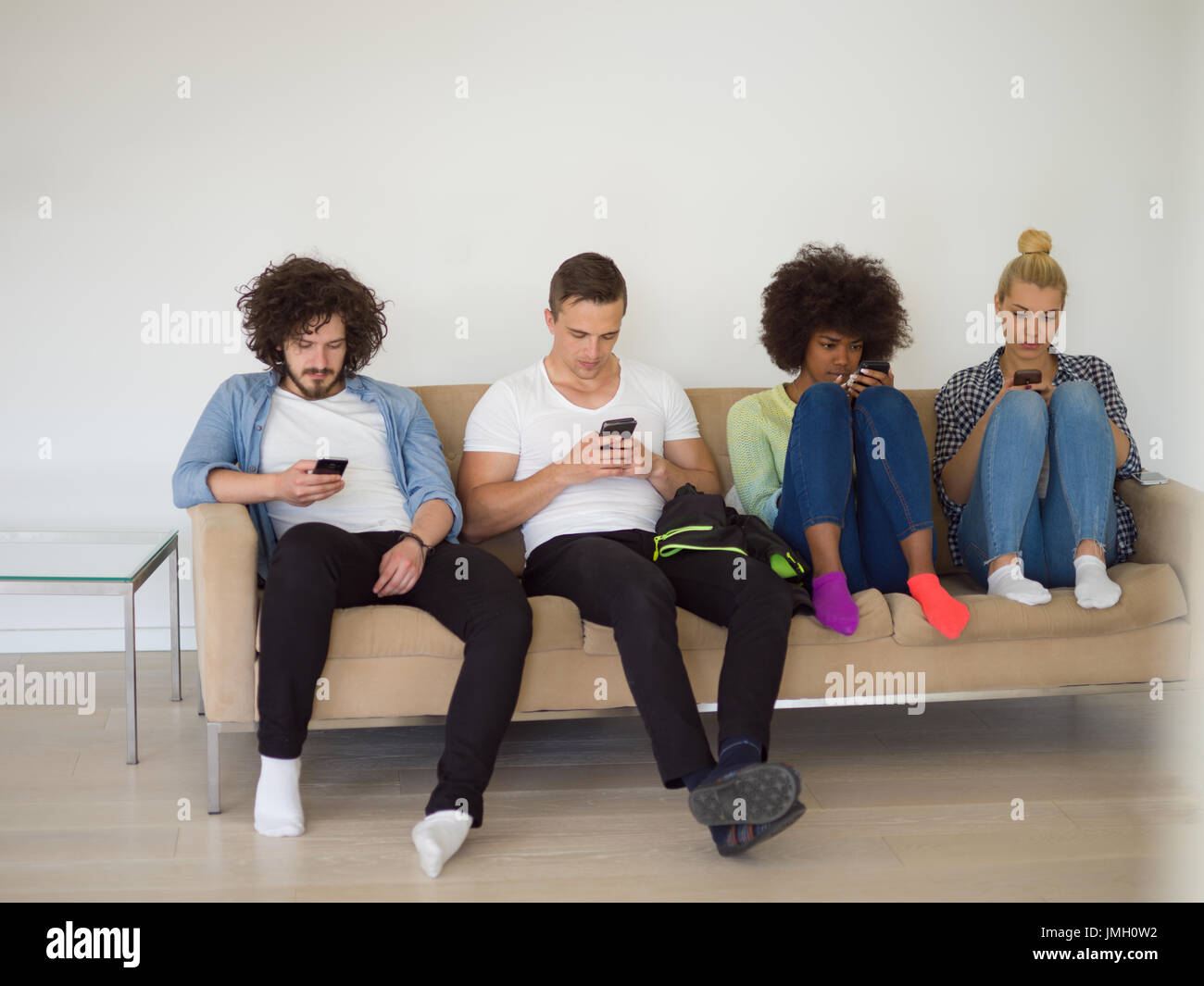 multiethnic group of young people sitting on a sofa at home,staring at ...