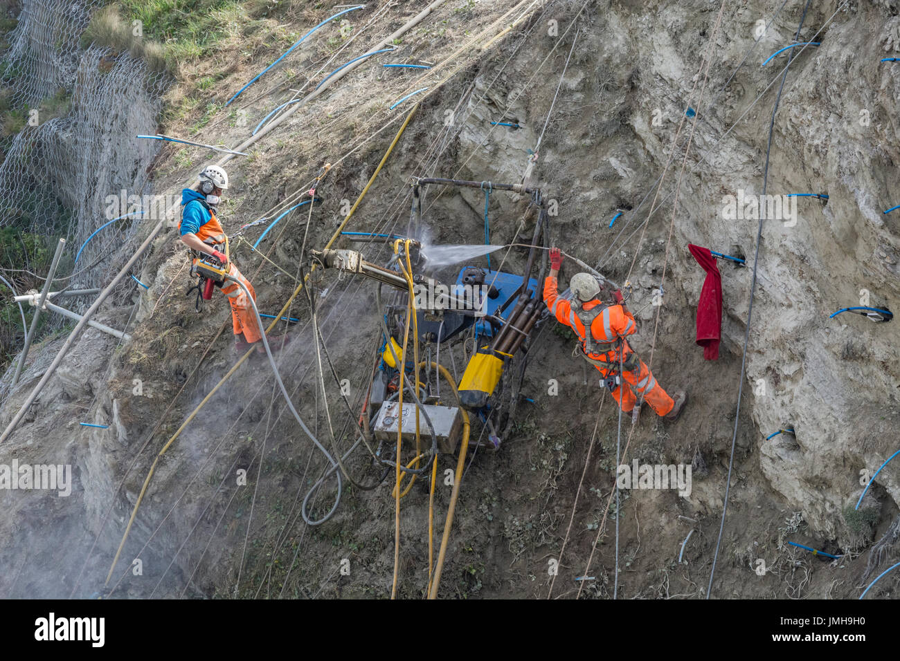 Telephoto shot of workmen drilling holes for cliff stabilisation rock ...
