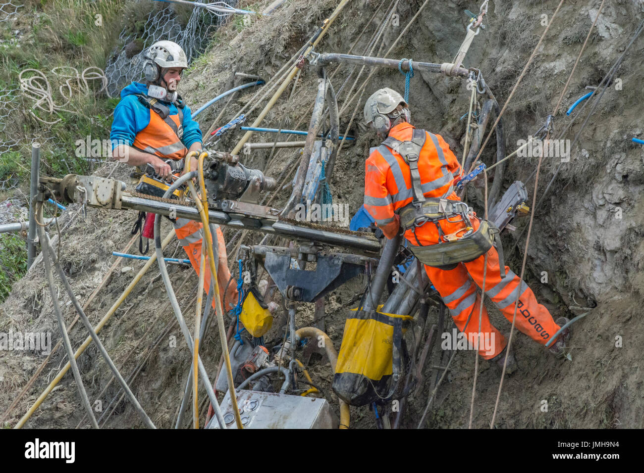 Telephoto shot of workmen drilling holes for cliff stabilisation rock ...