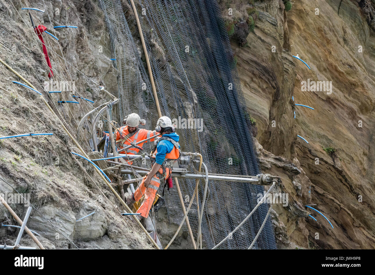 Telephoto shot of workmen drilling holes for cliff stabilisation rock ...
