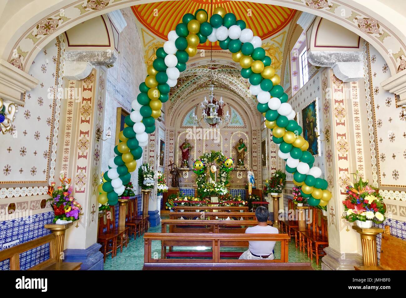 Man sitting in small, ornate church chapel decorated with balloon arch ...