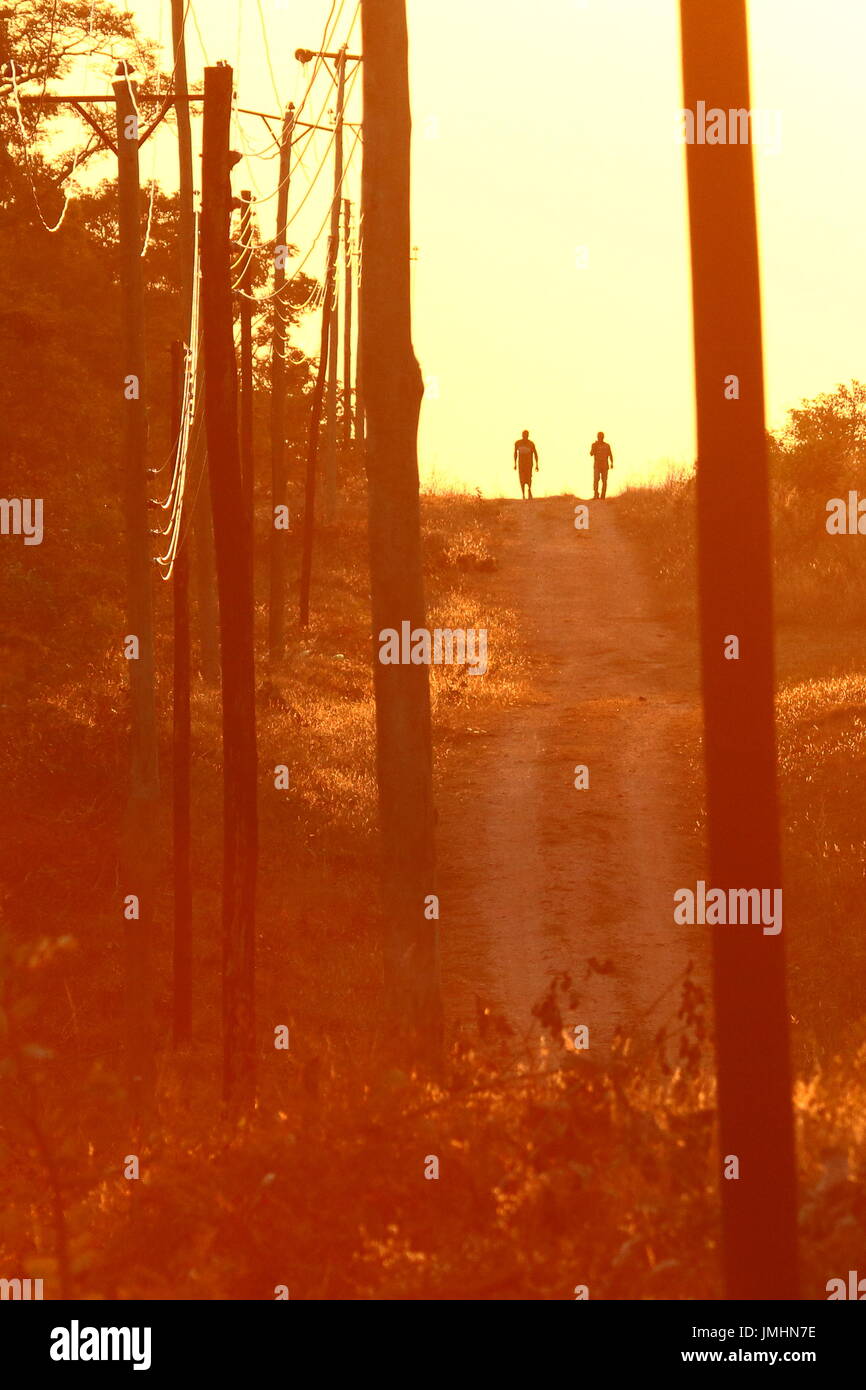 Two people walking in a rural African landscape at sunset. Leopard's ...