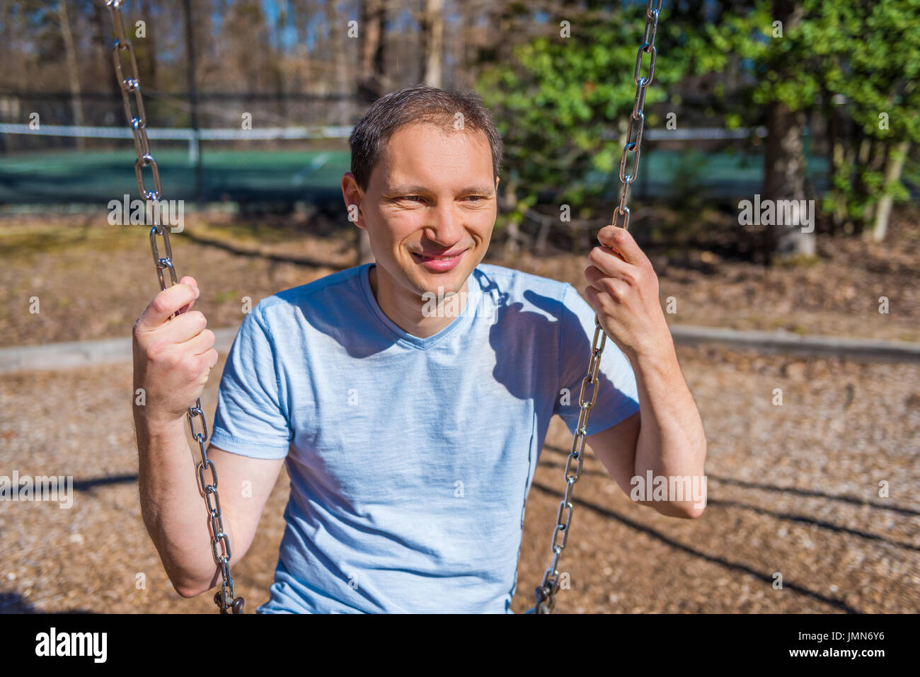 Young happy man on swing in playground smiling Stock Photo - Alamy
