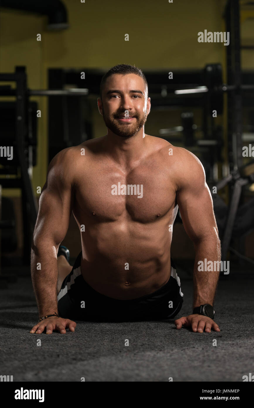 Muscular Man Stretches At The Floor In A Gym And Flexing Muscles ...