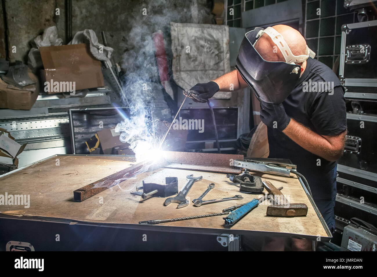 A bald, strong man in a black T-shirt welds a metal welding machine in ...