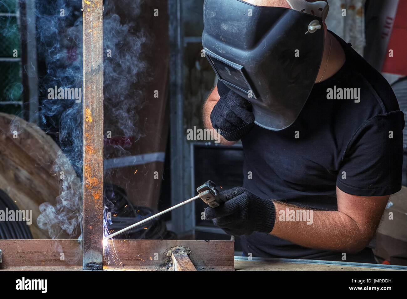 A bald, strong man in black work clothes cooking a metal product with a ...