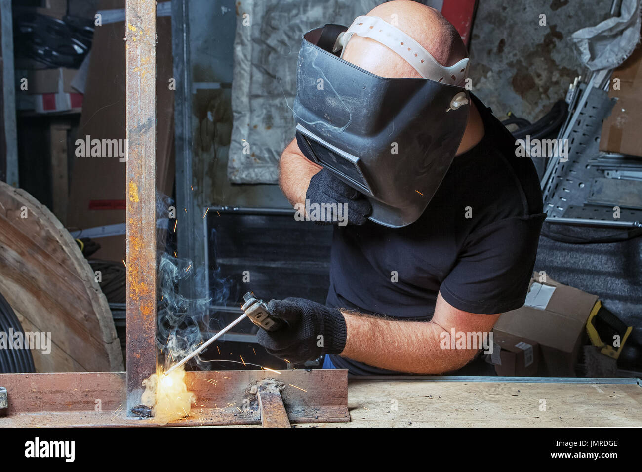 A bald, strong man in black work clothes is welding a metal arc welding ...
