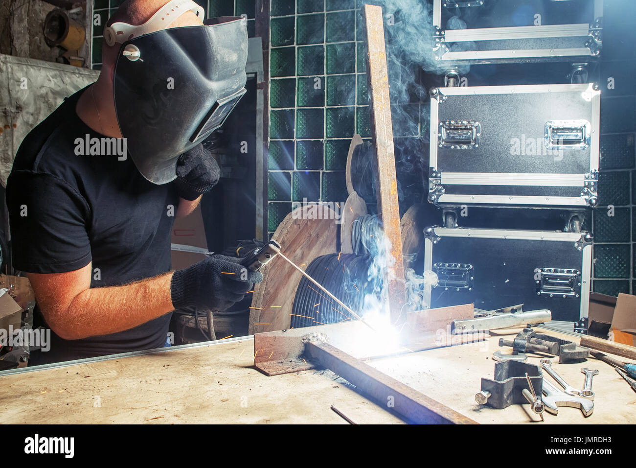 A bald, strong man in black work clothes welds a metal welding machine ...