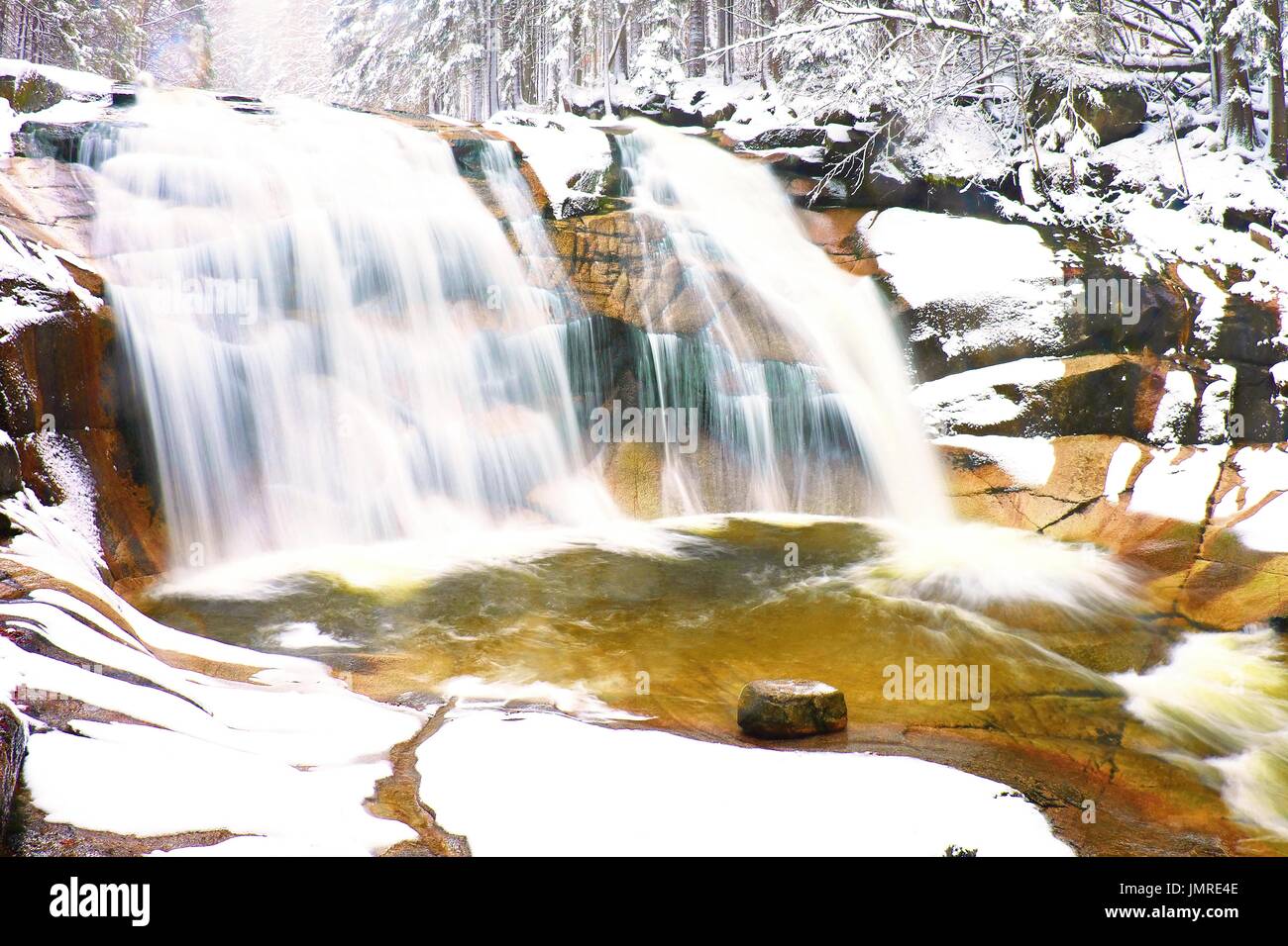 Winter view over snowy boulders to cascade of waterfall. Wavy water ...