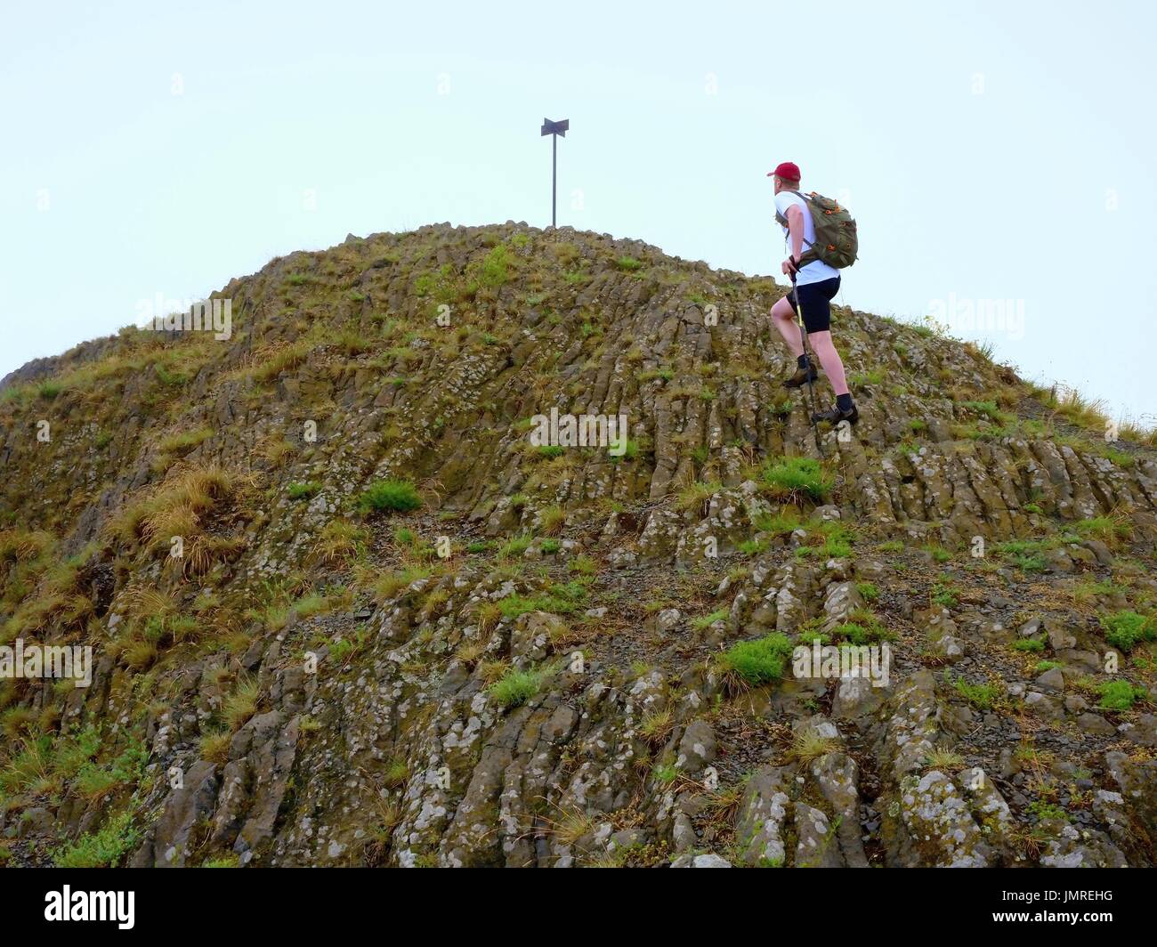 Hiker climbing on sharp peak of basalt formation. Long basalt poles of ...