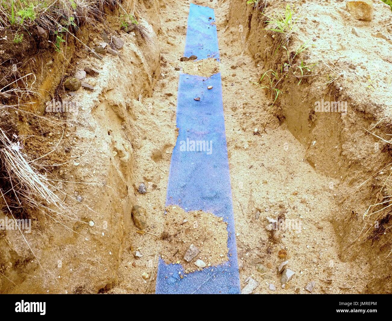 Trench with blue plastic protection tape. Marked of cables under gravel ...