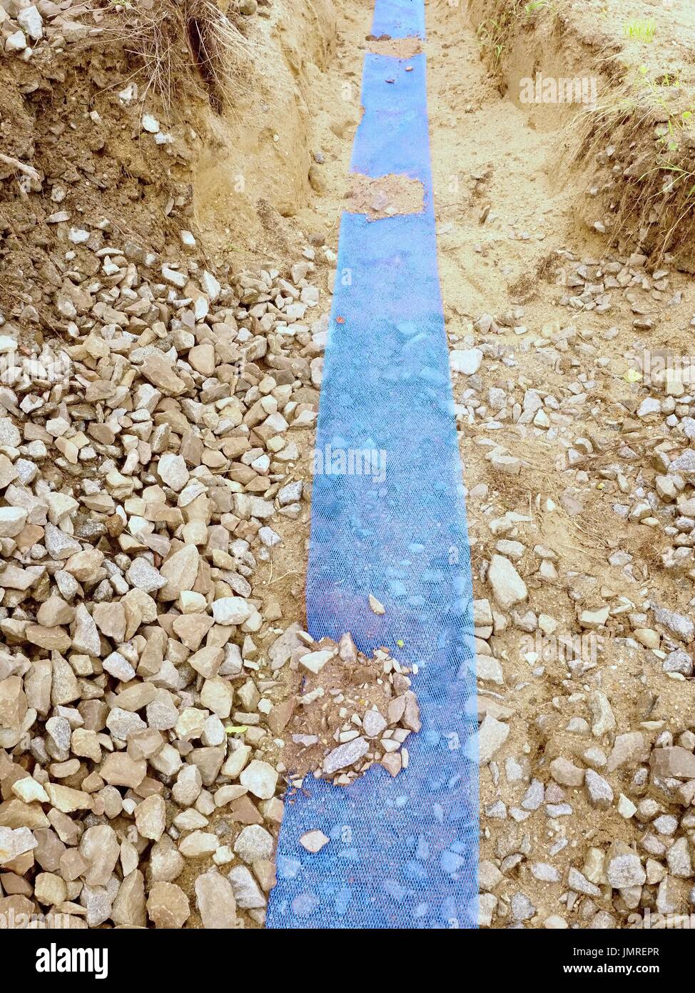 Trench with blue plastic protection tape. Marked of cables under gravel ...