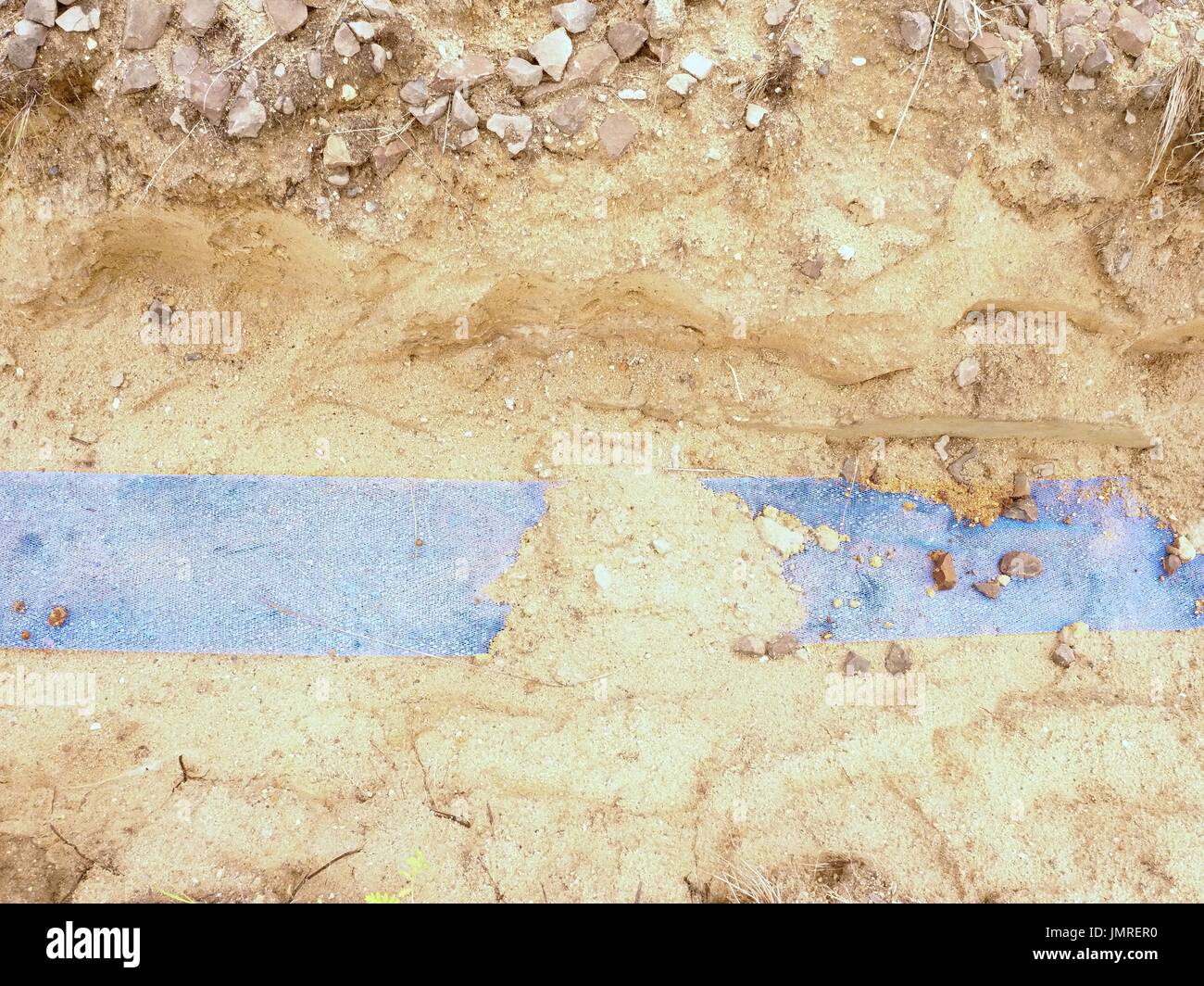 Trench with blue plastic protection tape. Marked of cables under gravel ...