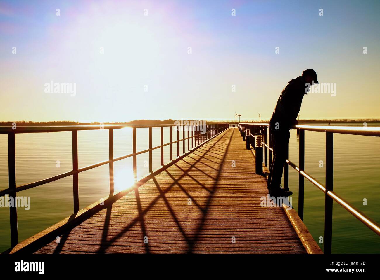 Alone man on pier and look over handrail into water. Sunny clear blue ...