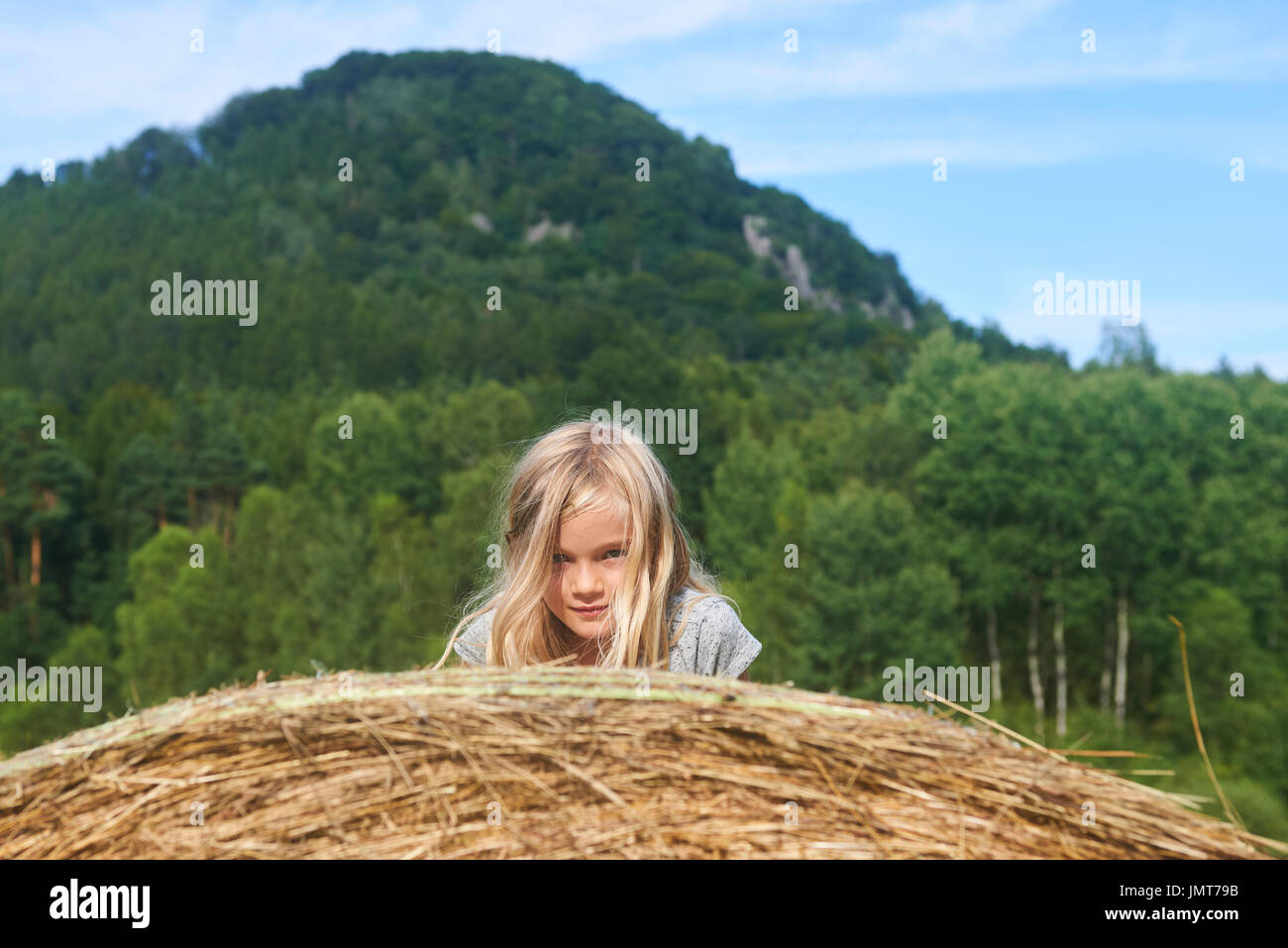 Child blond Girl by straw hay bale in field. Children summer activities ...