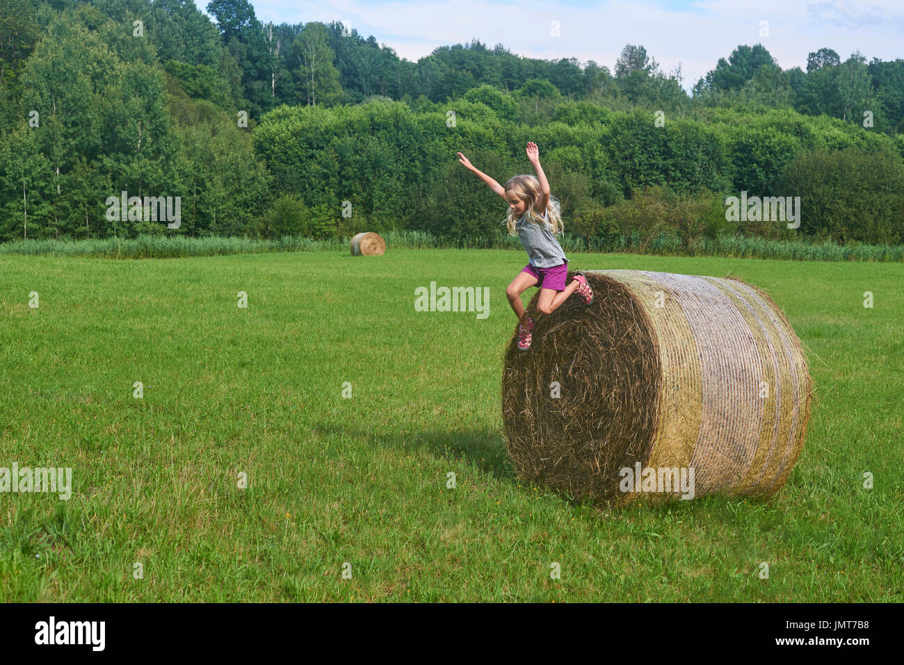 Child blond Girl by straw hay bale in field. Children summer activities ...