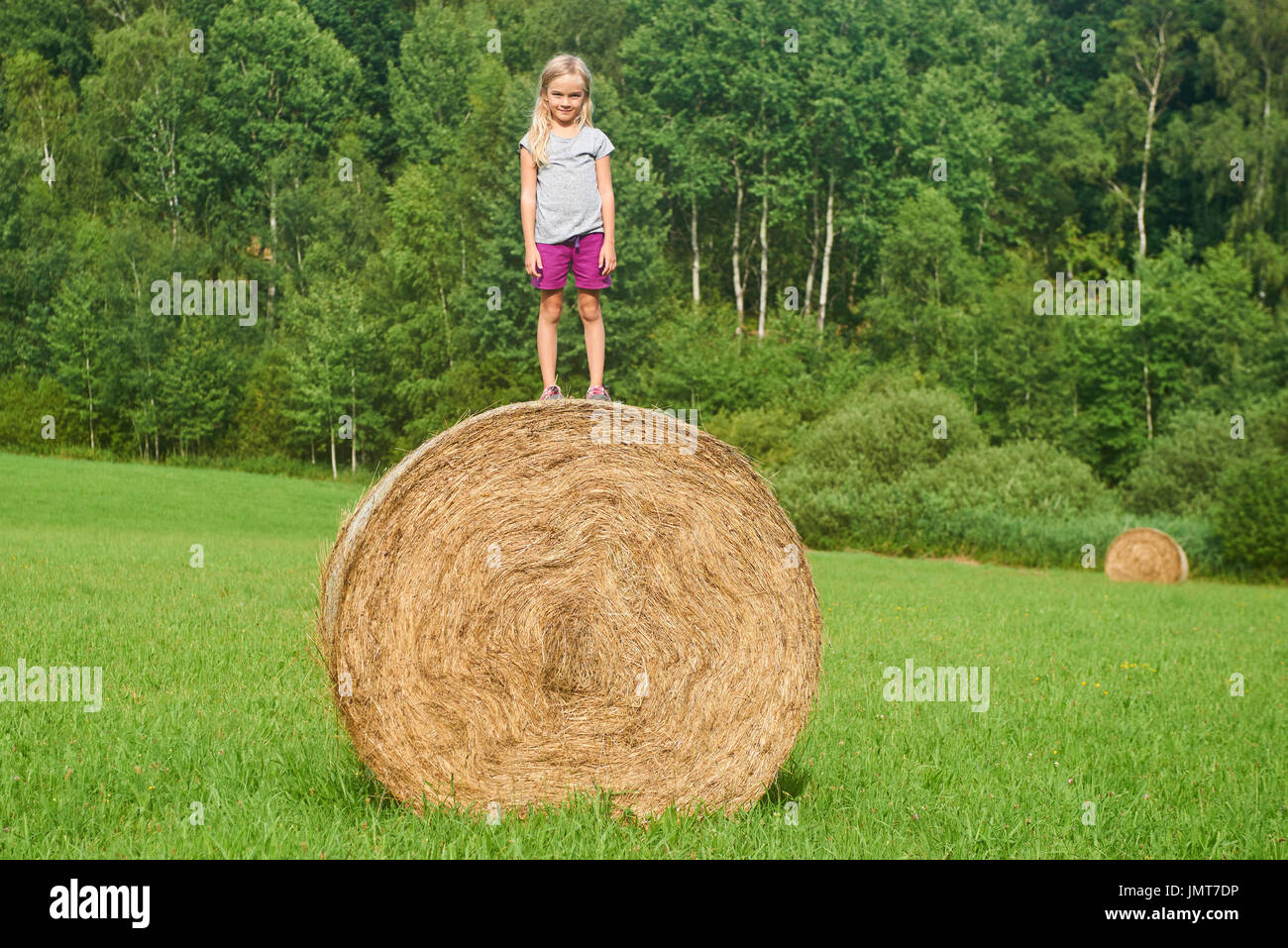 Child blond Girl by straw hay bale in field. Children summer activities ...