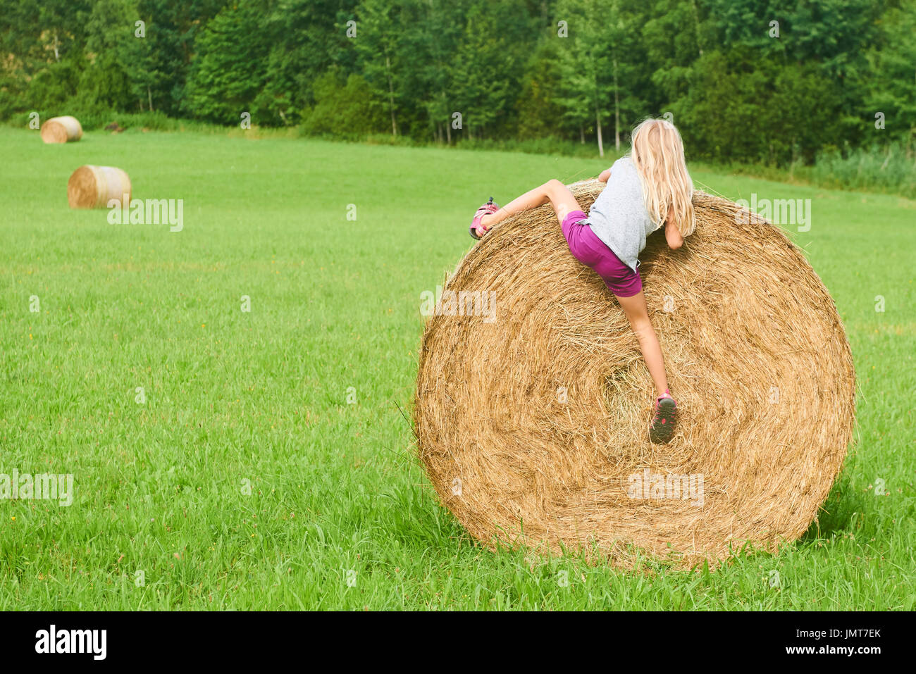 Child blond Girl by straw hay bale in field. Children summer activities ...