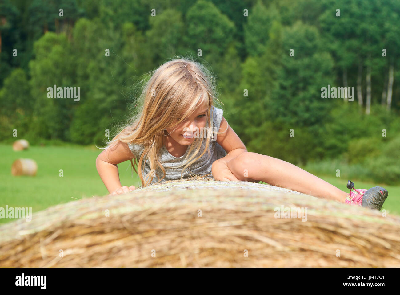 Child blond Girl by straw hay bale in field. Children summer activities ...