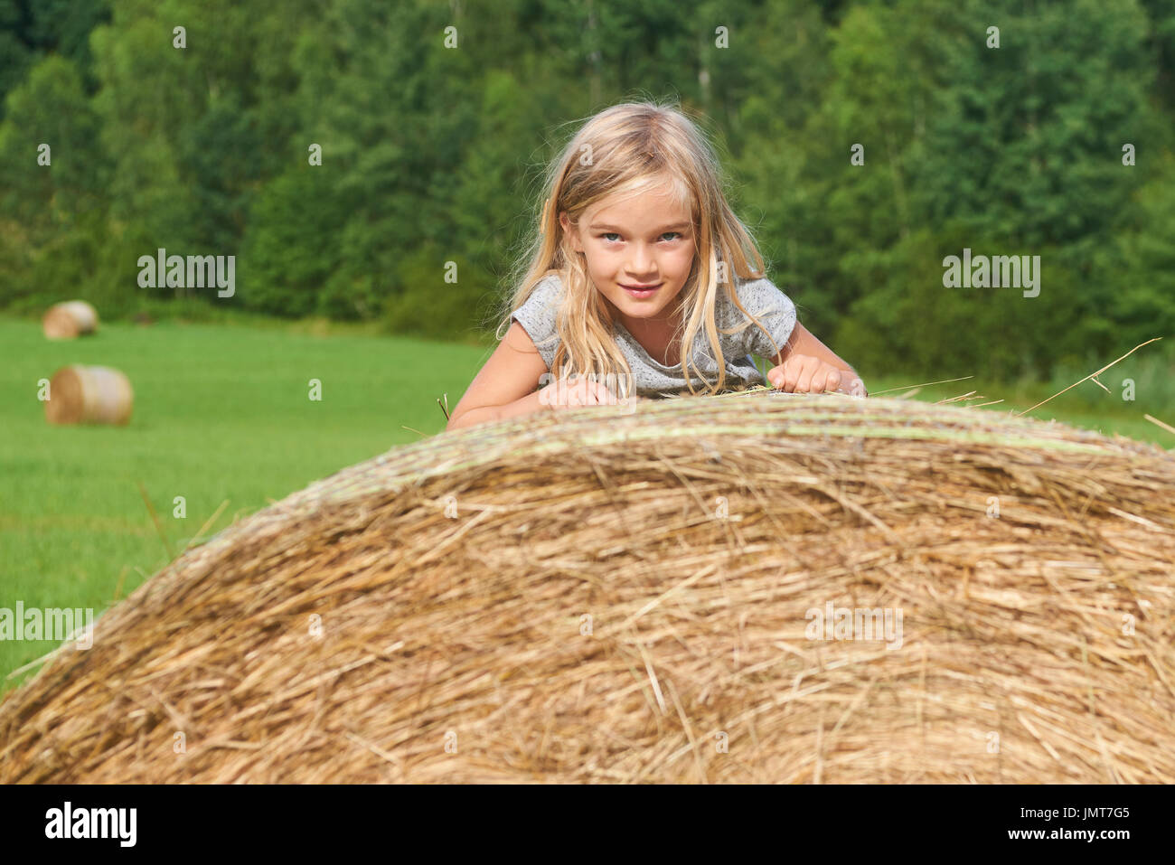 Child blond Girl by straw hay bale in field. Children summer activities ...