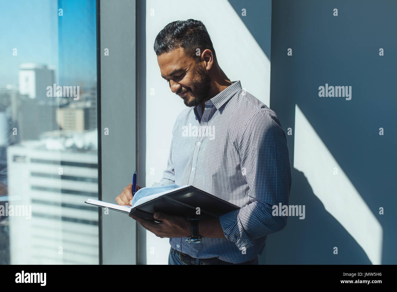 Young businessman writing notes in diary standing at the window in ...