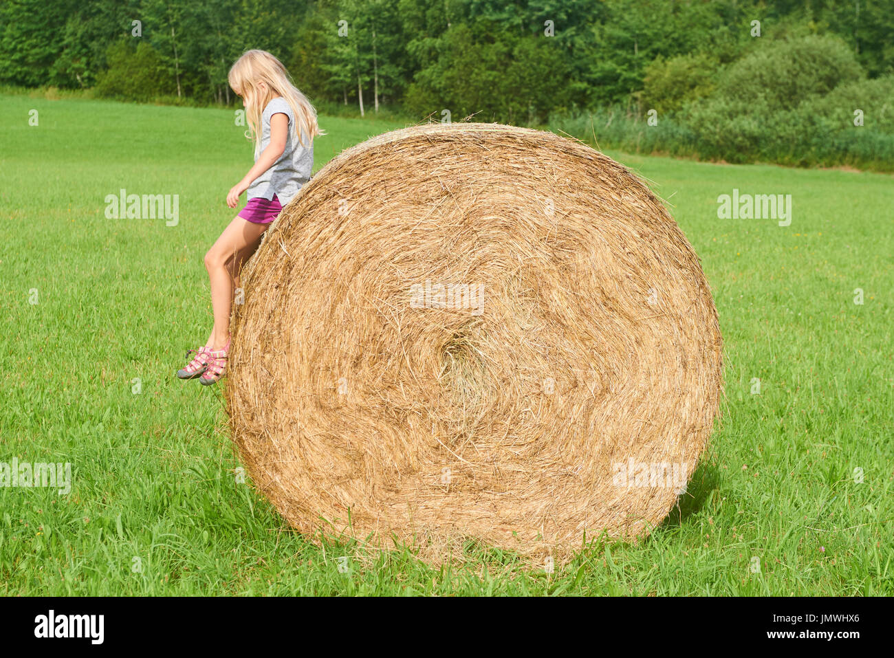 Child blond Girl by straw hay bale in field. Children summer activities ...