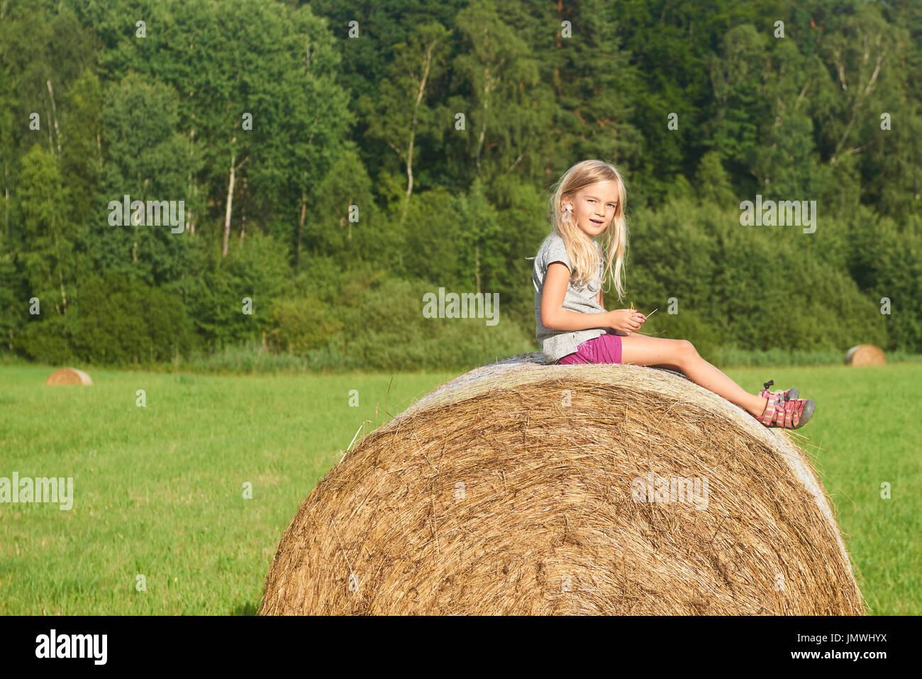 Child blond Girl by straw hay bale in field. Children summer activities ...