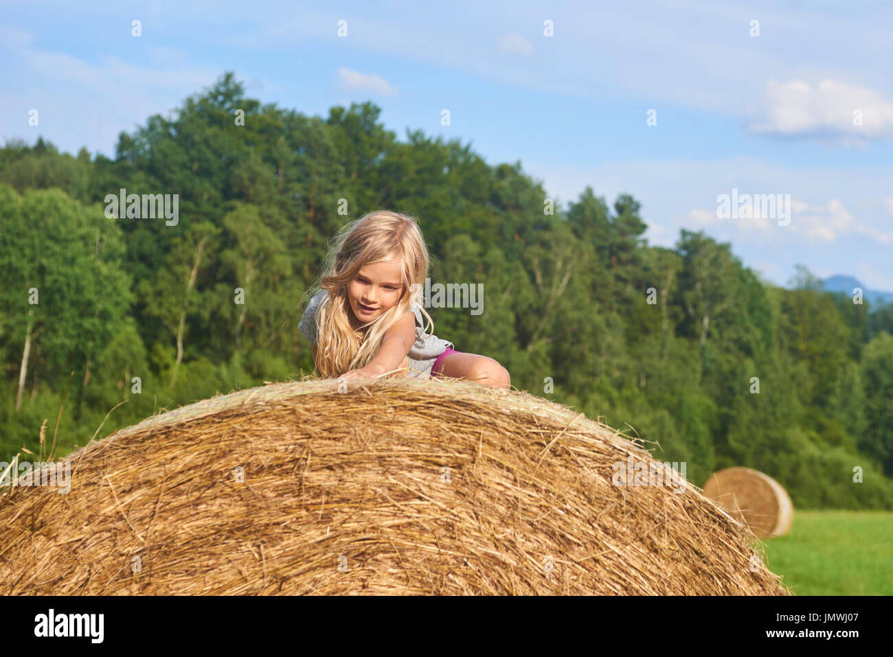 Child blond Girl by straw hay bale in field. Children summer activities ...