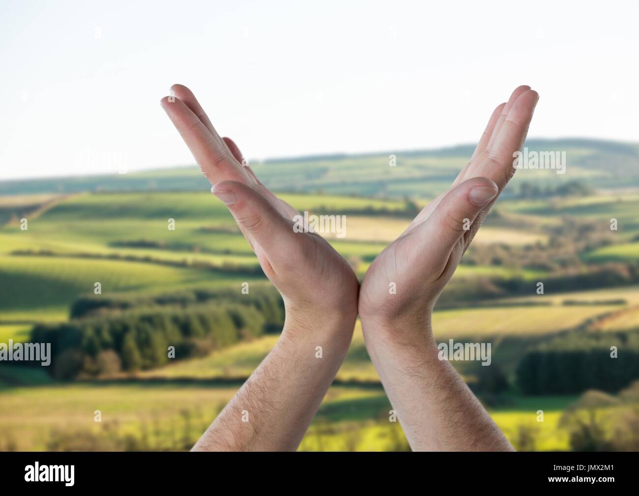 Digital composite of Hands opened in V shape over green landscape Stock ...