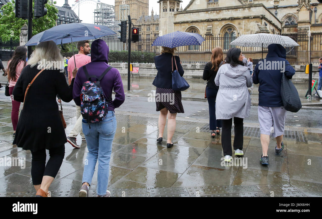 People take shelter from the rain under umbrellas in Westminster after ...