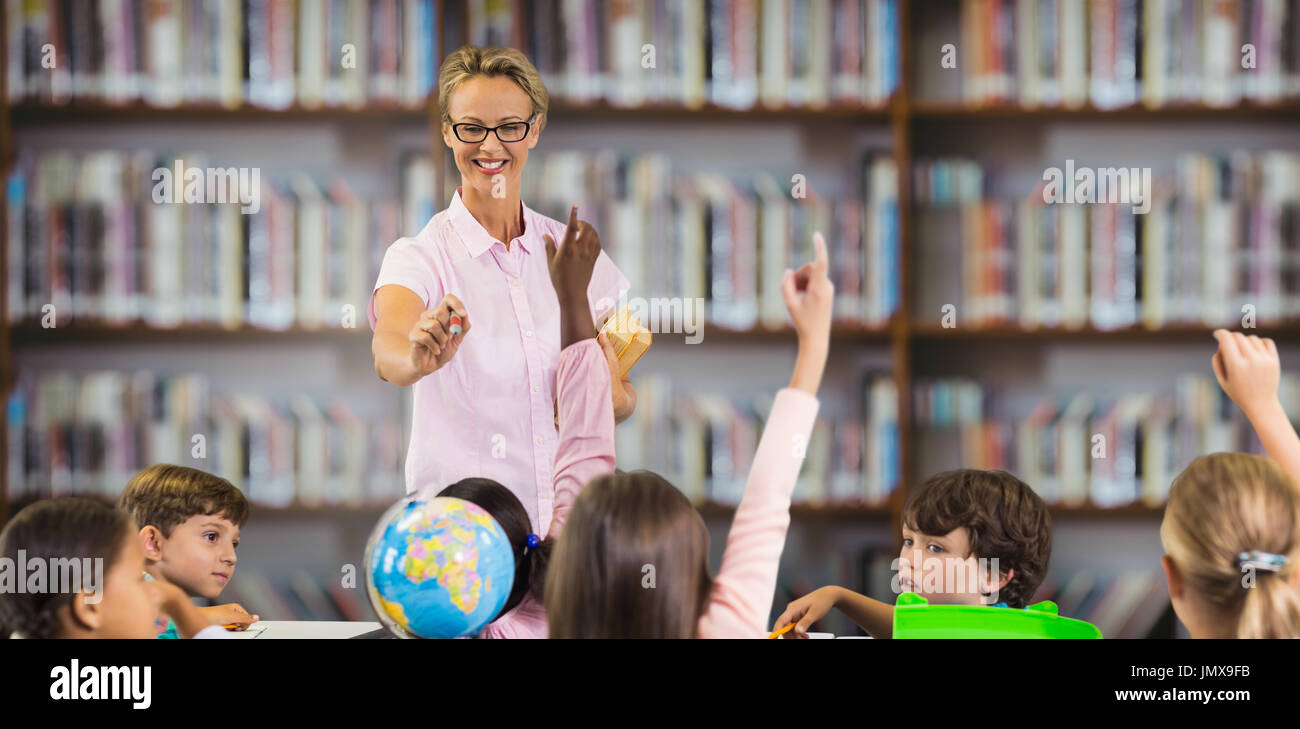 Students raising hands while teacher teaching against library shelf ...