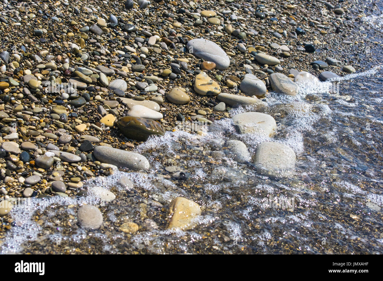 sea pebble beach with multicoloured stones, transparent waves with foam ...