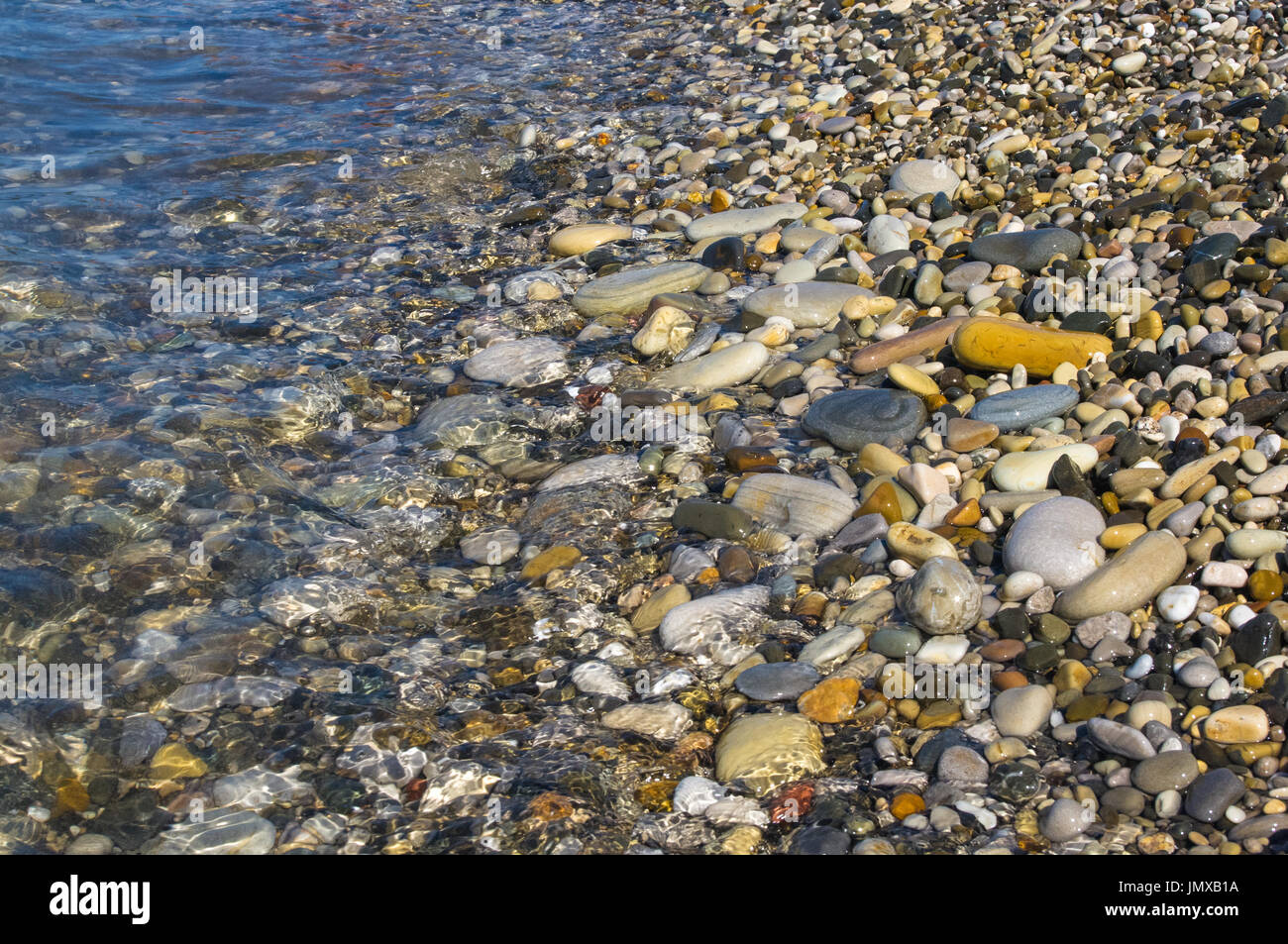 sea pebble beach with multicoloured stones, transparent waves with foam ...