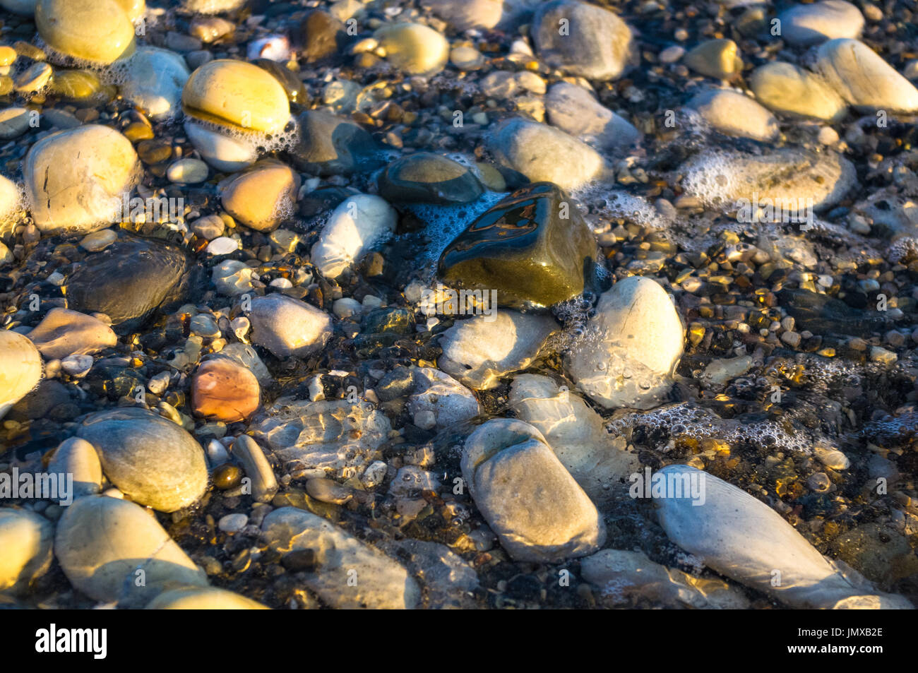 sea pebble beach with multicoloured stones, transparent waves with foam ...