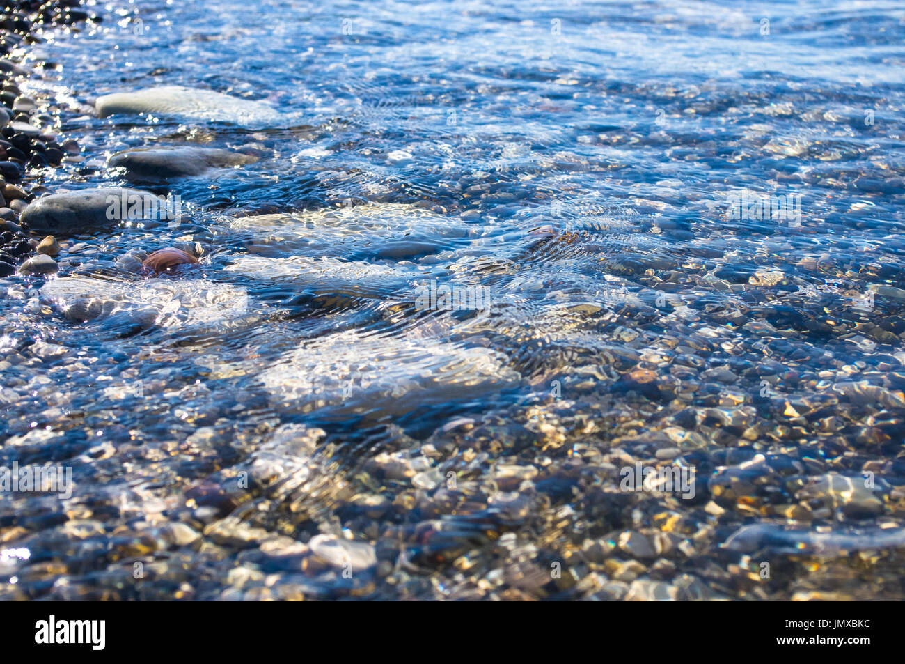 sea pebble beach with multicoloured stones, transparent waves with foam ...