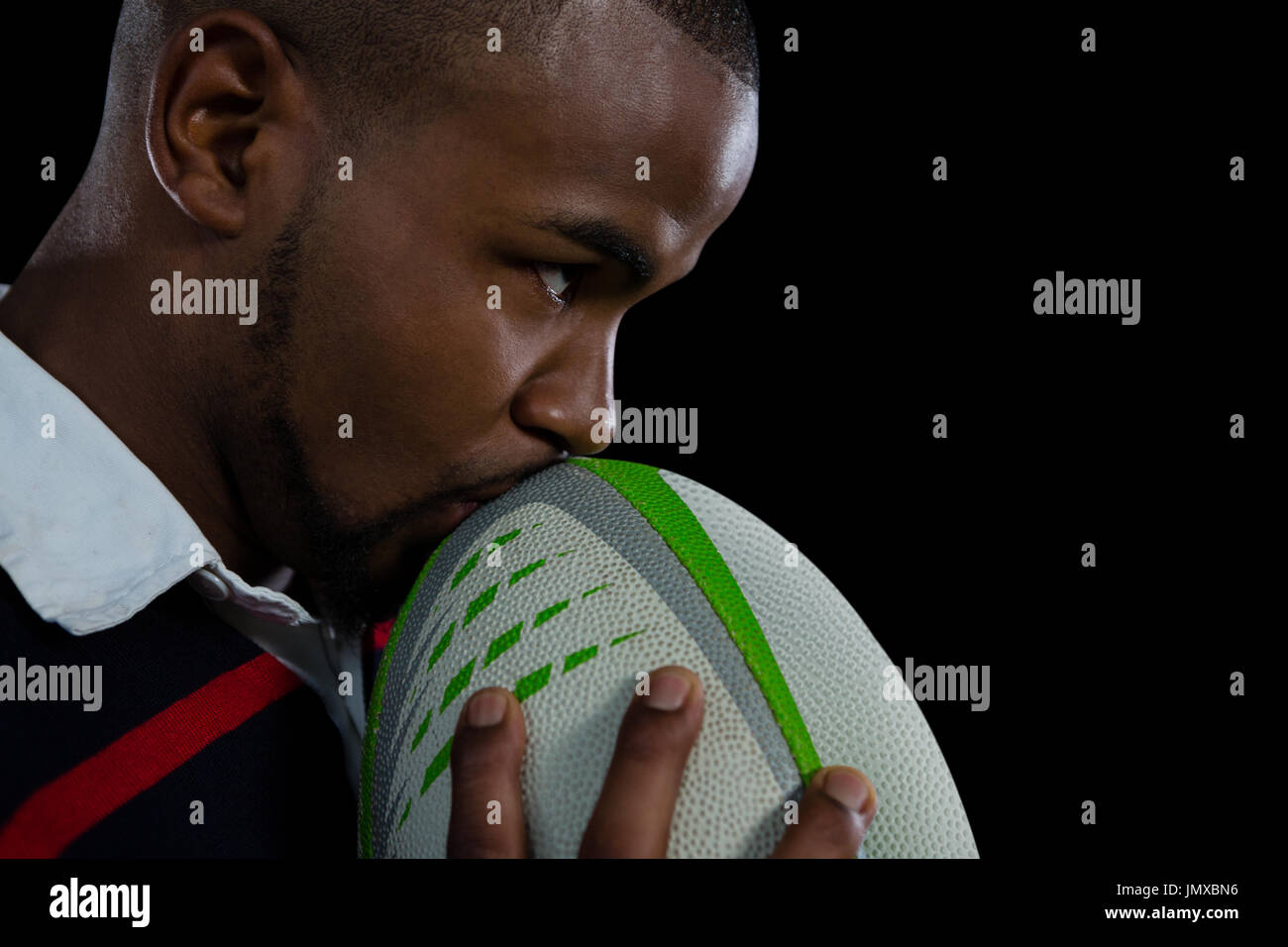 Close up of male player kissing rugby ball against black background ...
