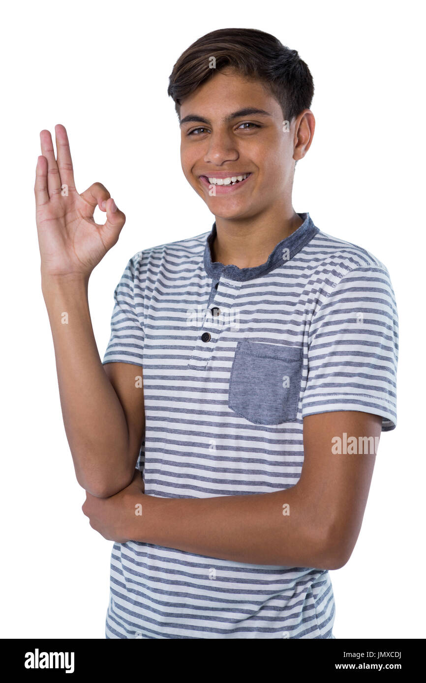 Smiling teenage boy gesturing okay hand sign against white background ...