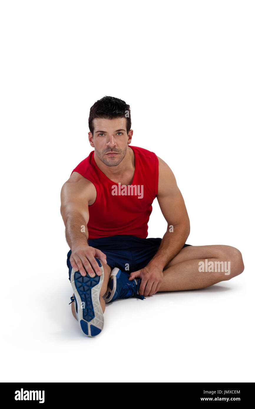 Portrait of sportsman stretching legs while exercising against white ...