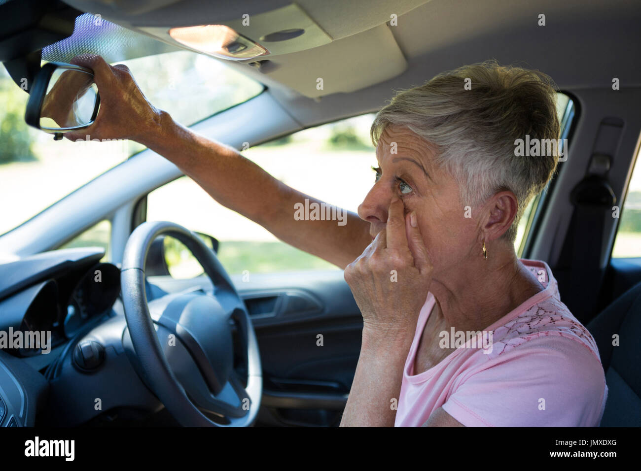 Active senior woman looking into rear view mirror while driving a car ...