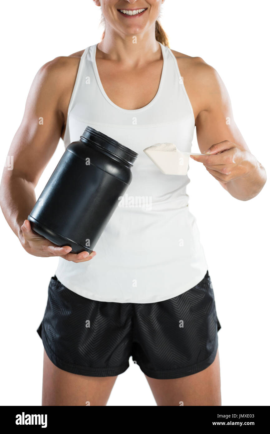 Mid section of smiling female athlete taking supplement powder while ...