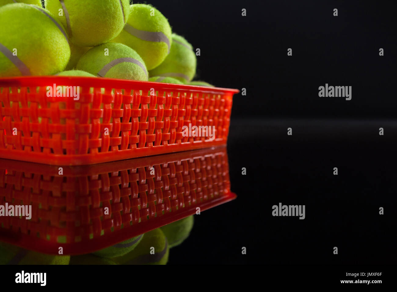 Pile of fluorescent yellow tennis balls in red plastic basket with ...