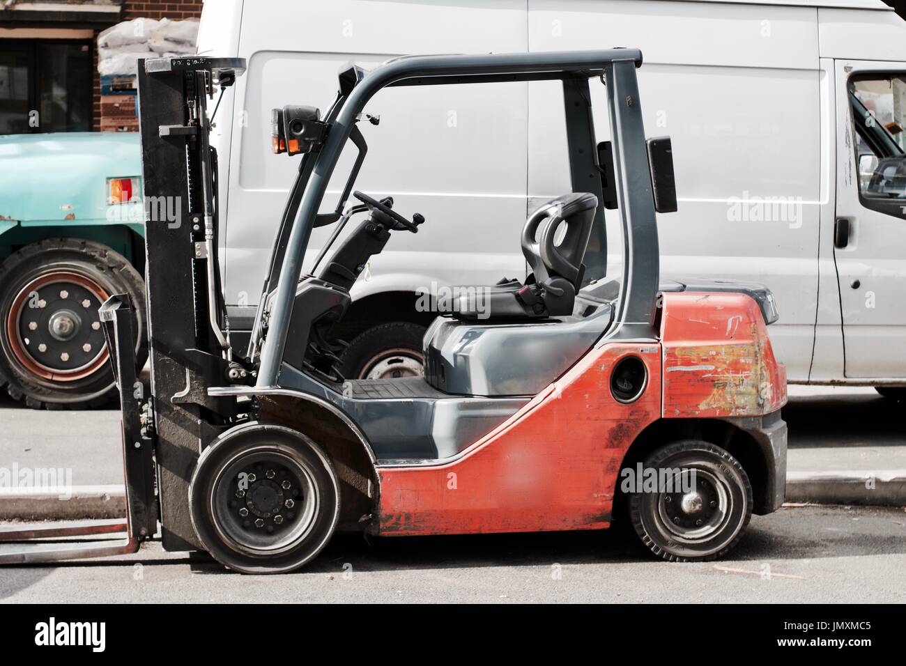 Old red outdoor lift truck near white big van and blue reach truck ...