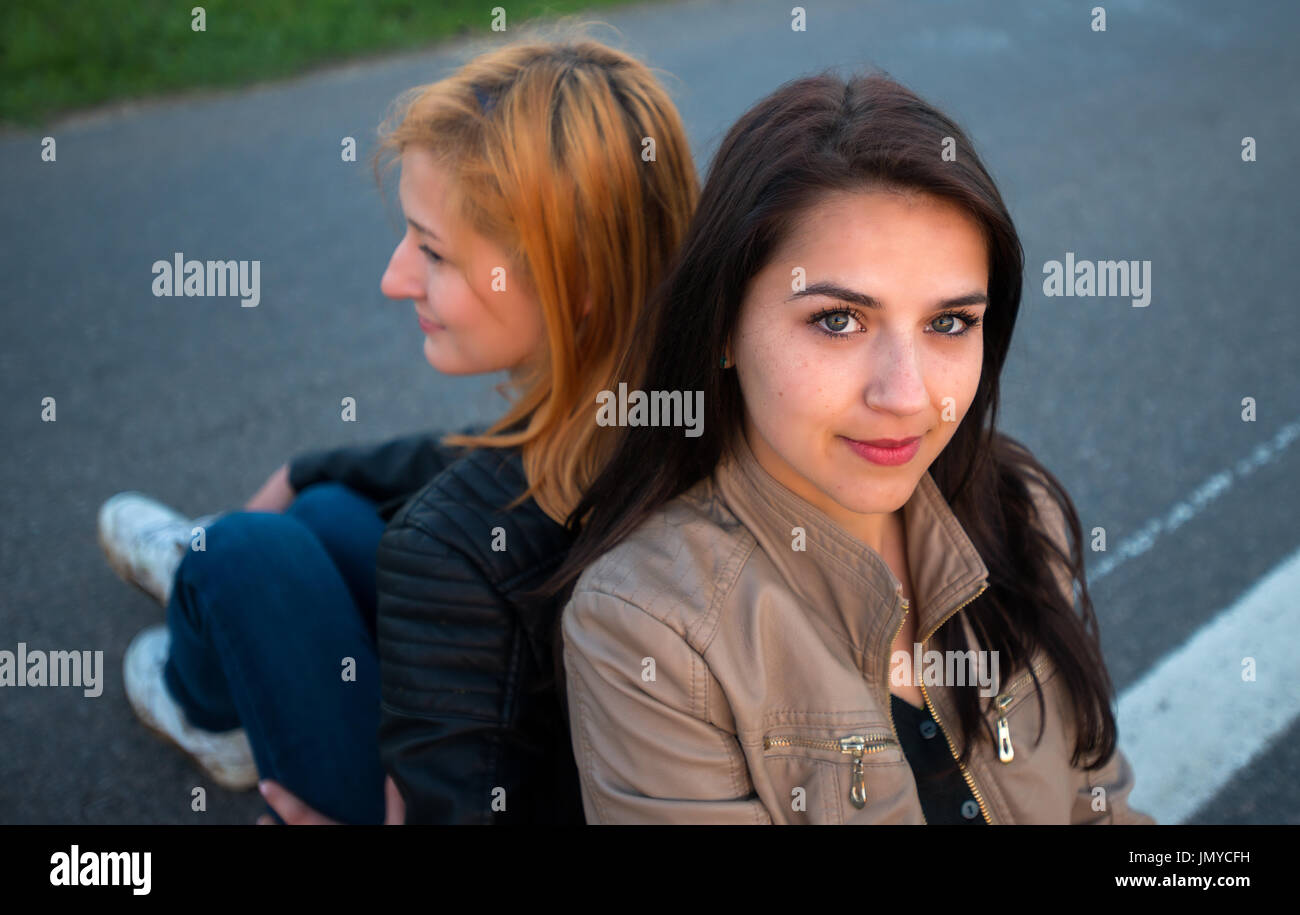 Two girls sitting back to back Stock Photo - Alamy