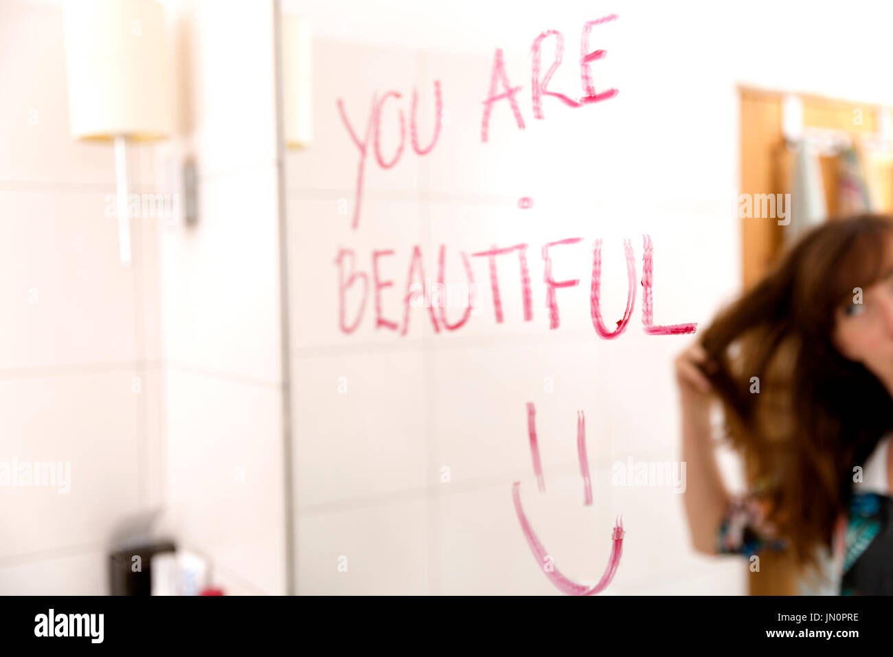 Women encouraging herself by writing words you are beautiful on mirror ...