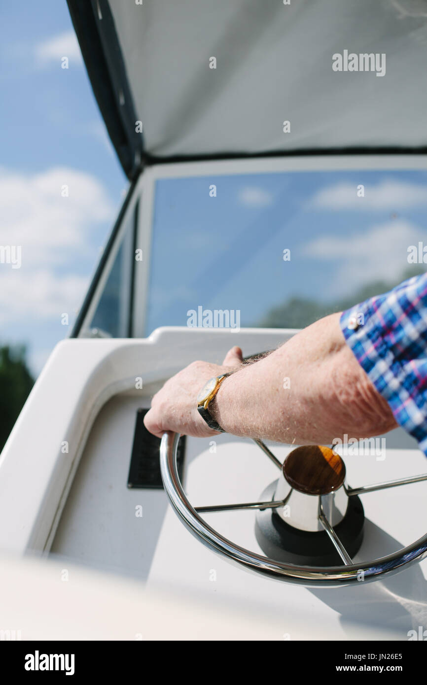 Close up of a steering wheel of a boat on a river with a man's hand on ...