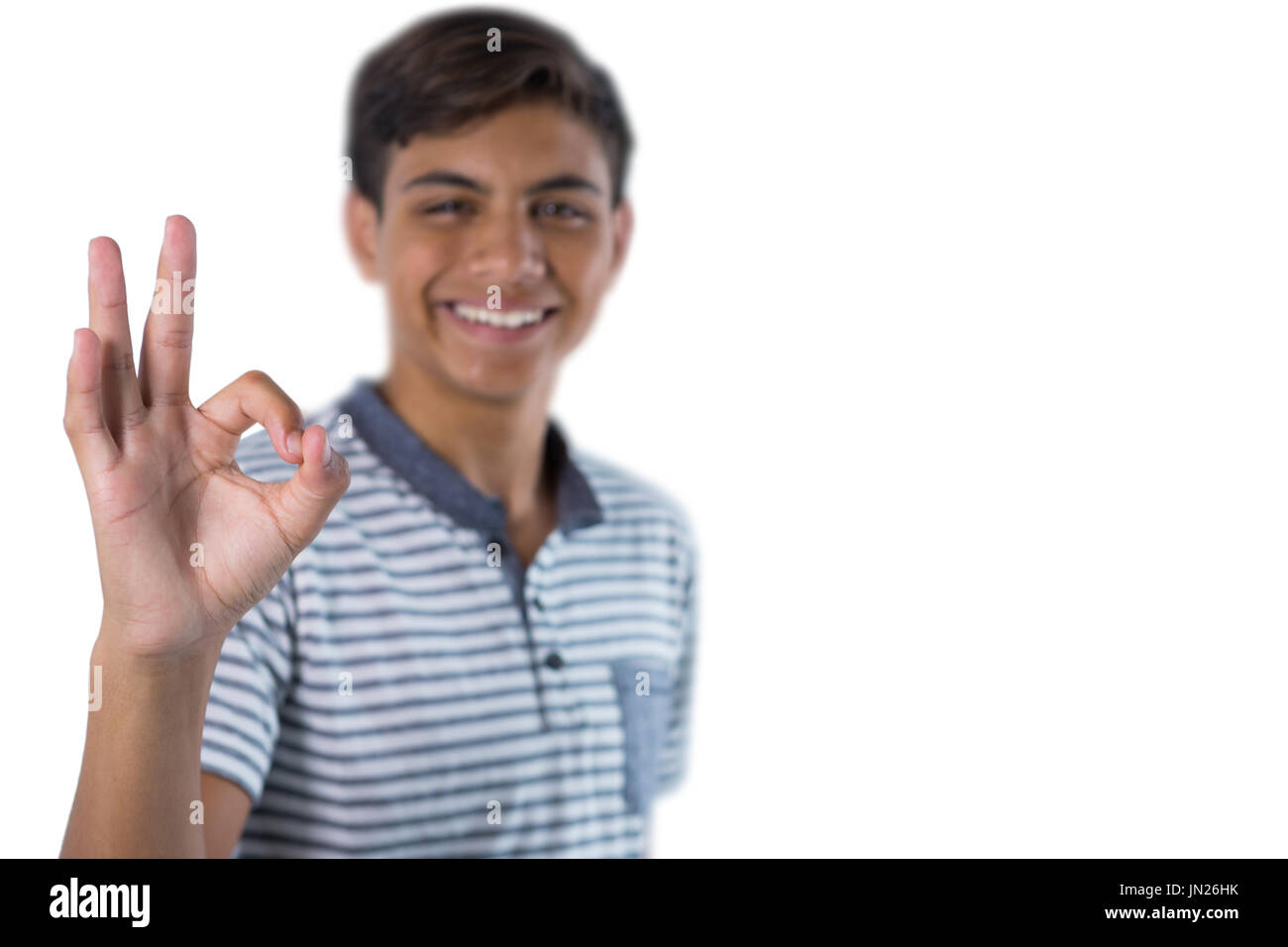 Smiling teenage boy gesturing okay hand sign against white background ...